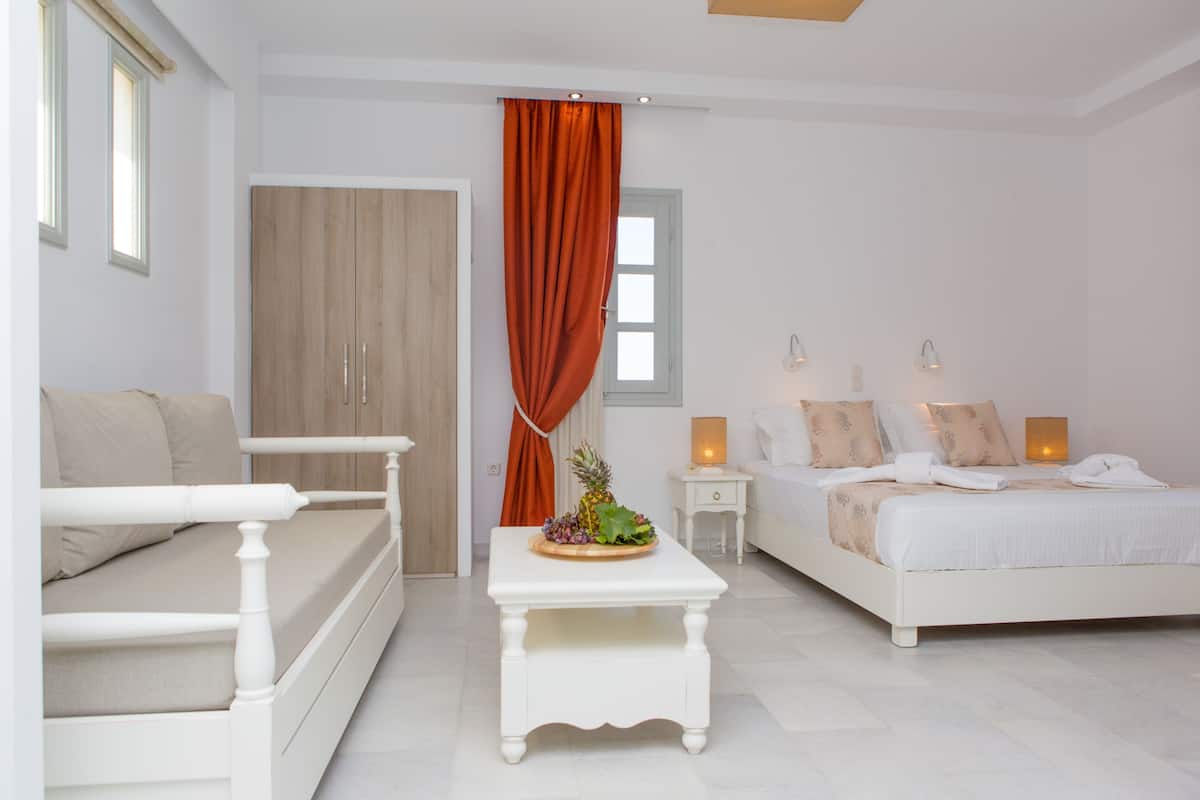 Um quarto com cama, sofá, uma mesinha com frutas e criado-mudo com luminárias.