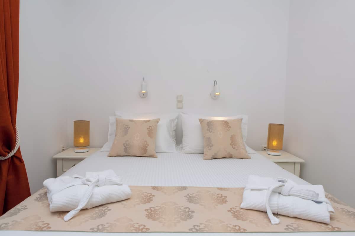 Quarto de hotel com cama, duas luminárias laterais, mesa de cabeceira e um roupão sobre a cama.
