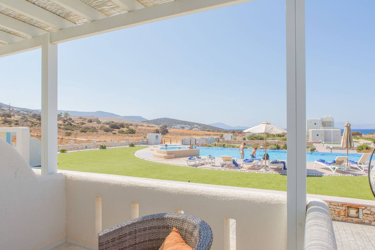 Uma área de piscina com espreguiçadeiras e guarda-sóis, vista desobstruída para o mar e paisagem gramada ao fundo.