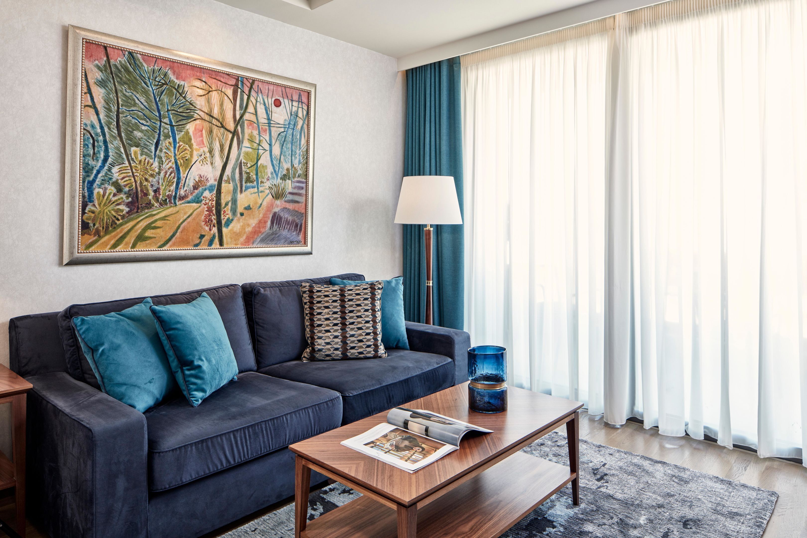 Uma sala de estar moderna com um sofá escuro, almofadas estampadas, uma mesa de centro de madeira e um quadro na parede.