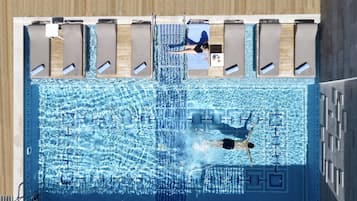 Piscina com uma pessoa nadando, cadeiras de descanso e um deck de madeira.