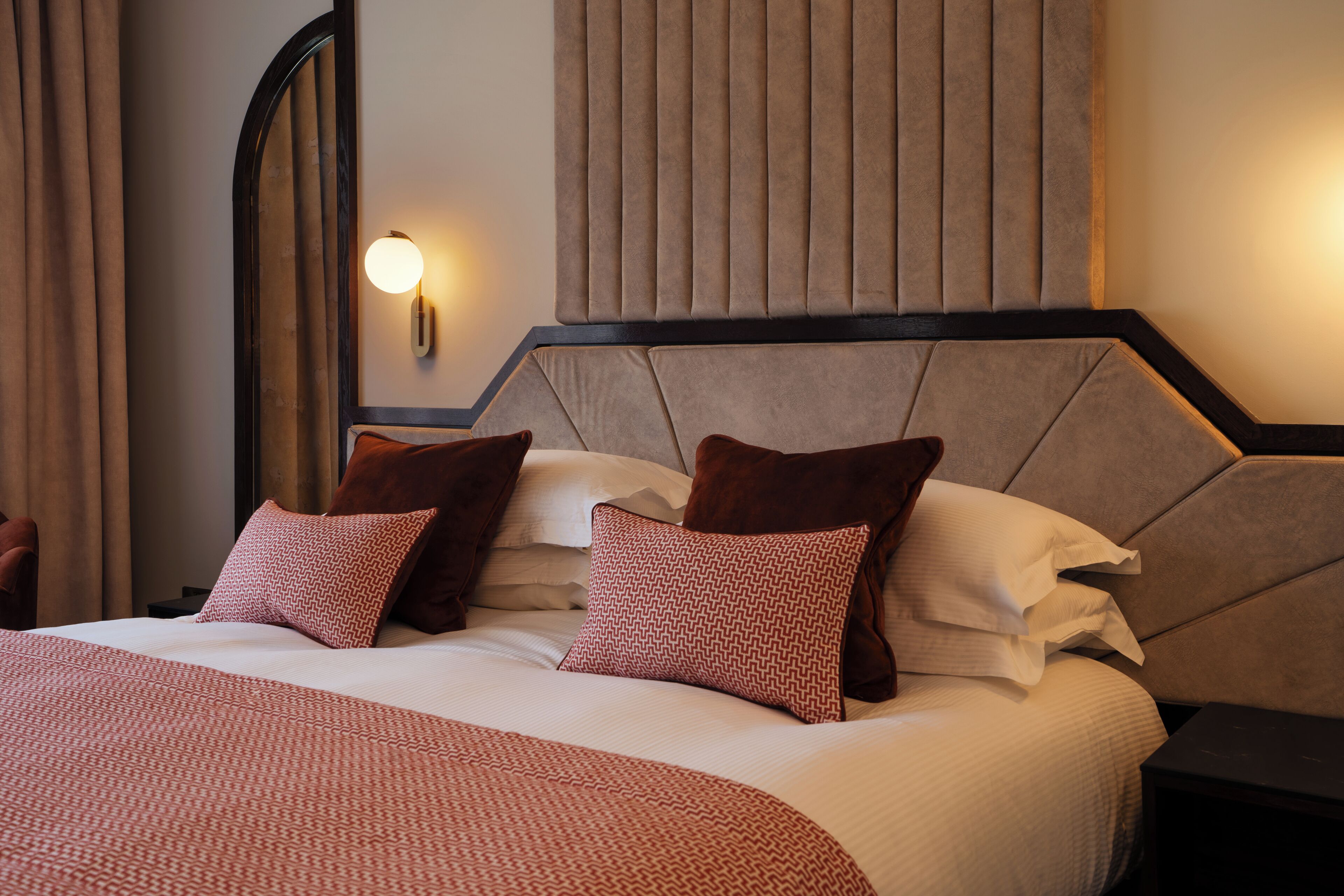 Cama bem arrumada com almofadas estampadas e cabeceira com ripas verticais.