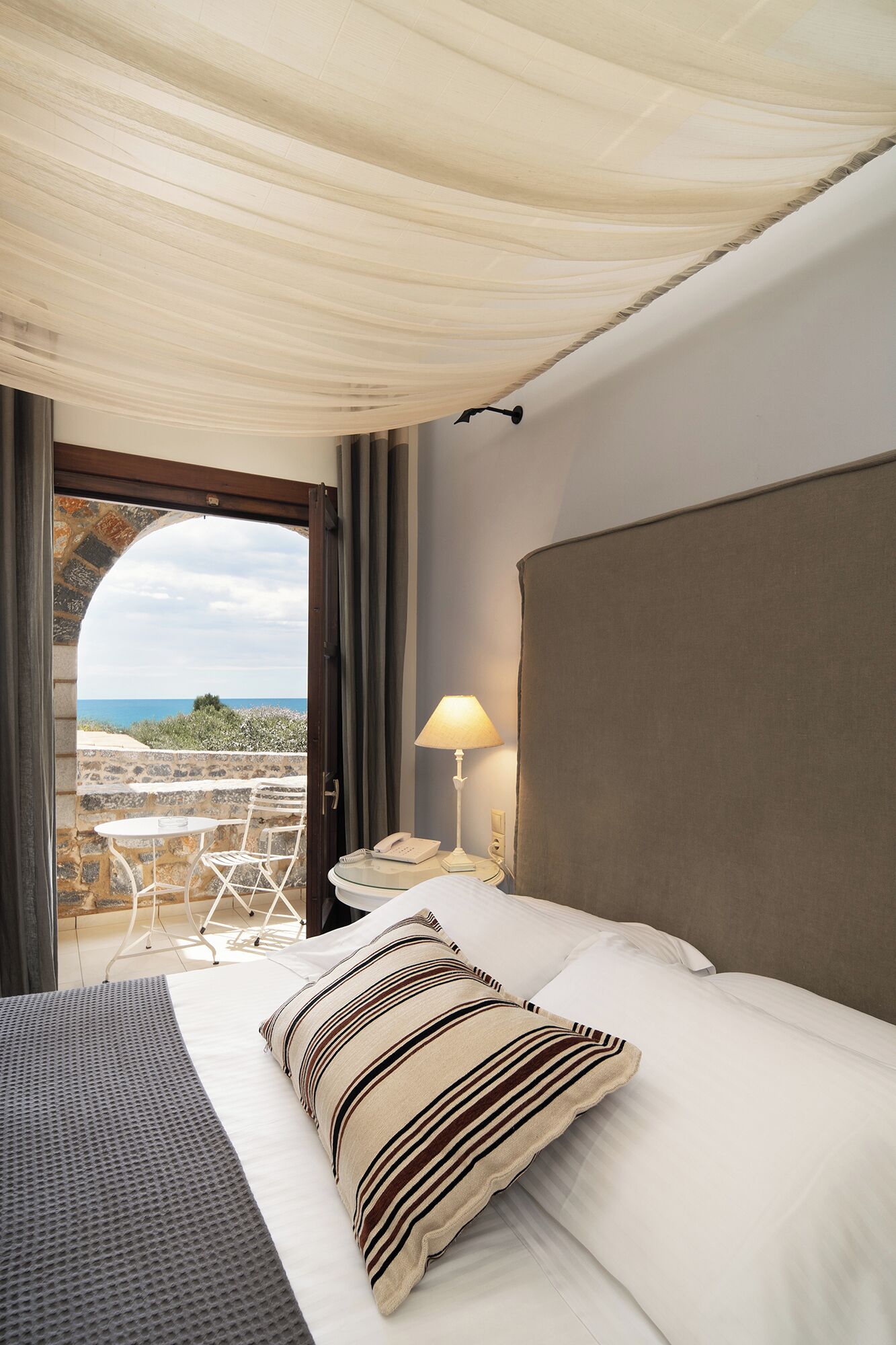 Quarto de hotel com cama, luminária, telefone e vista para o mar.