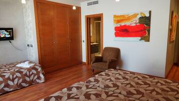 Quarto com duas camas, guarda-roupa de madeira, uma cadeira, um quadro e televisão.