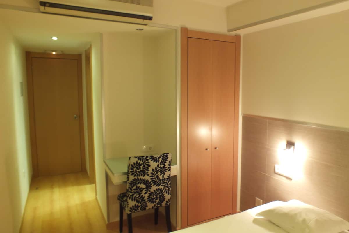 Quarto de hotel com uma cama, uma escrivaninha e um guarda-roupa.