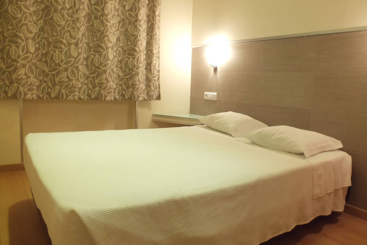 Quarto de hotel com cama, mesa de cabeceira e luminária fixada na parede.