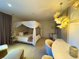 Quarto de hotel moderno com cama de dossel, escrivaninha, cadeira e luminária decorativa na parede.