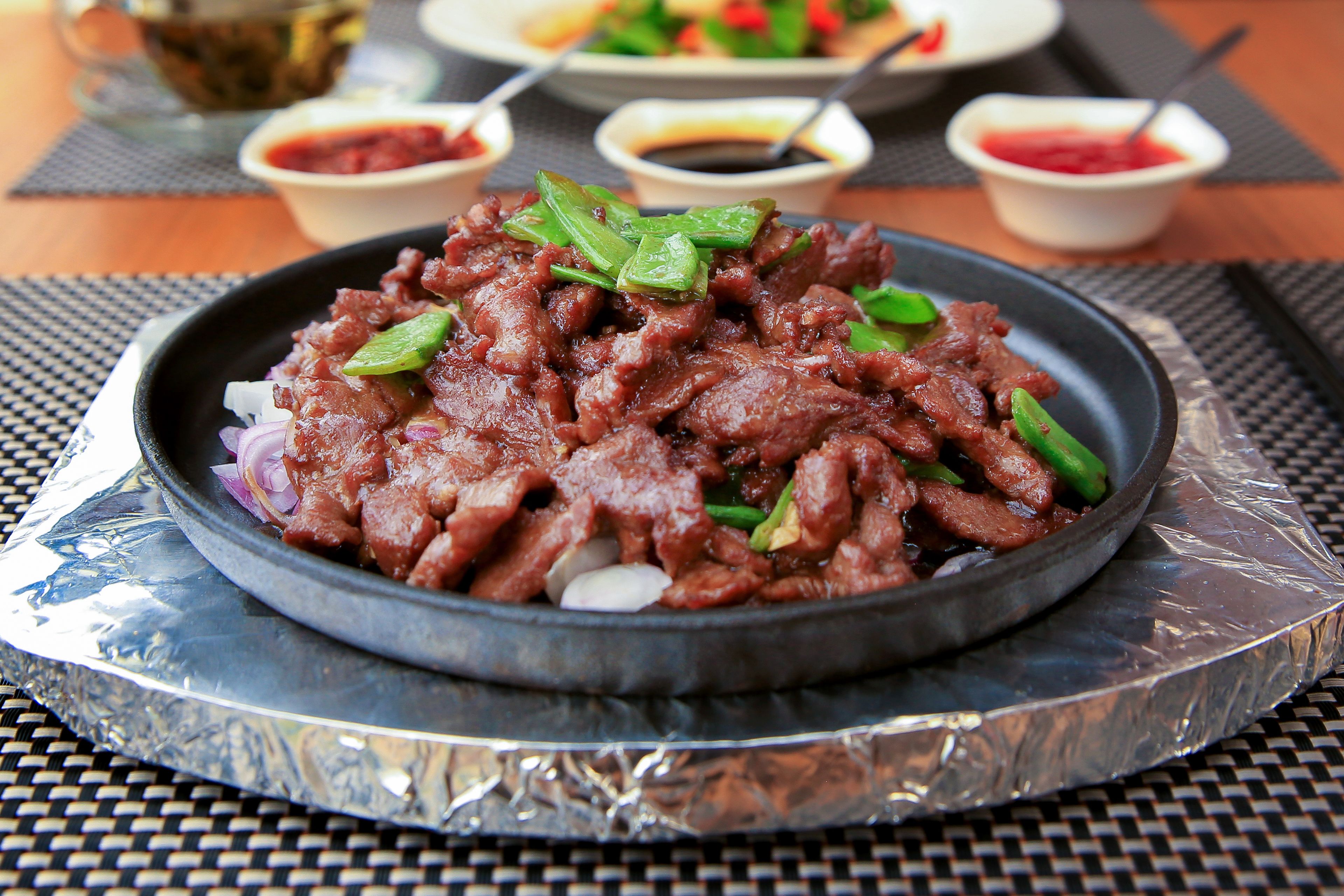 Prato de carne coberto com cebolinha e cebola roxa, servido em um prato preto com papel alumínio embaixo.