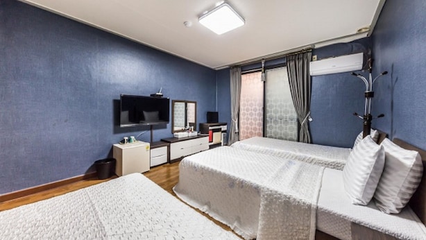 Quarto com duas camas, televisão, penteadeira, espelho e janela com cortinas.