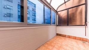 Um corredor com vista para um edifício moderno, uma janela com moldura metálica e piso de azulejos.