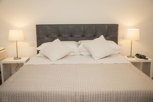 Uma cama bem arrumada com cabeceira estofada, duas luminárias laterais e um telefone na mesinha de cabeceira.
