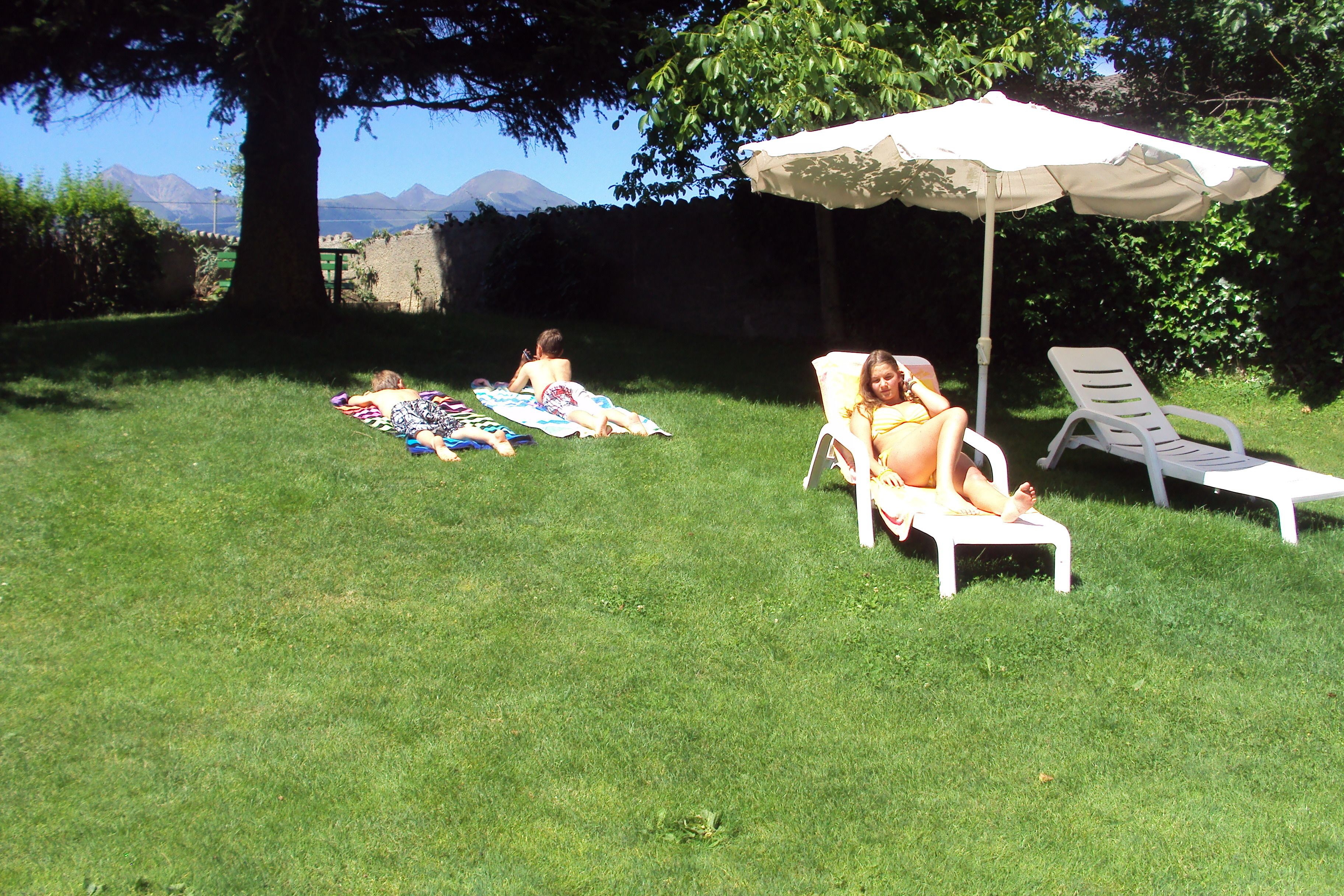 Uma área externa com grama, cadeiras de descanso e um grande guarda-sol para sombra.