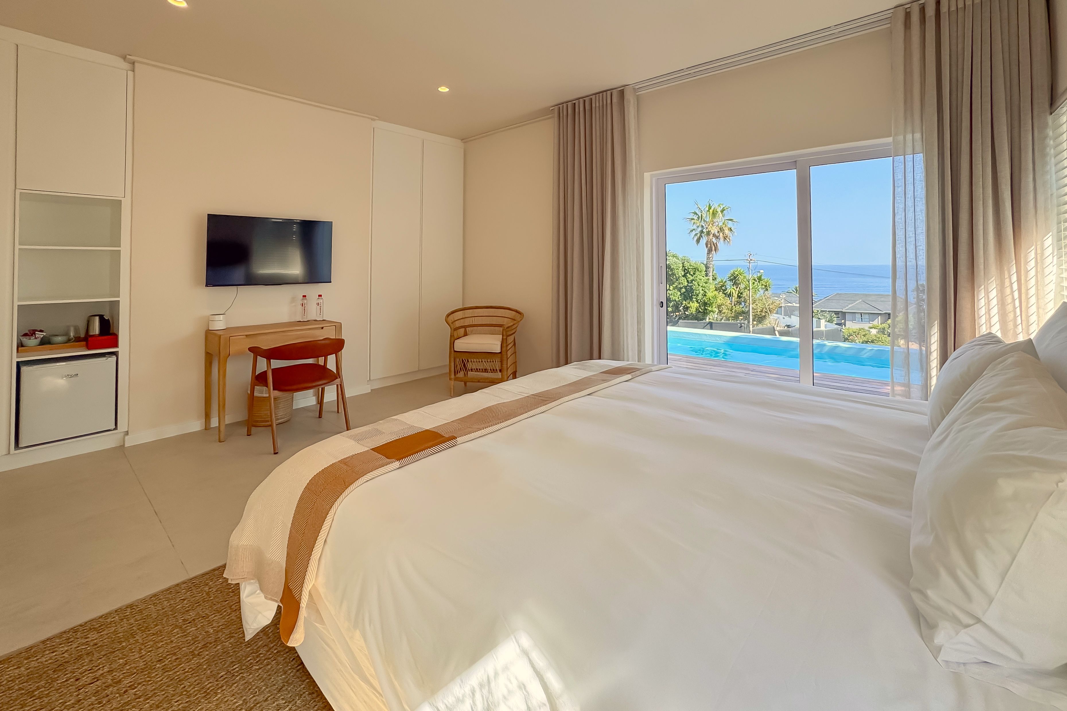 Quarto de hotel com uma cama grande, escrivaninha com cadeira, televisão e vista para o oceano.