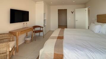 Quarto de hotel com cama, escrivaninha, cadeira, televisão e guarda-roupa.
