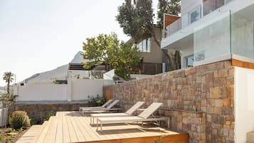 Uma área externa moderna com deck de madeira, cadeiras de estar e parede de pedra.