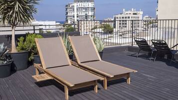 Um terraço no telhado com duas cadeiras de madeira para relaxar, plantas em vasos e vista para a paisagem urbana.
