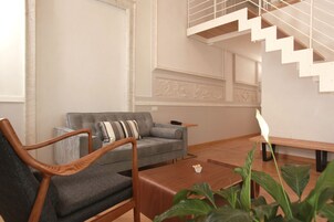 Uma sala de estar moderna com um sofá cinzento, mesa de centro de madeira e escada com guardaílos brancos.
