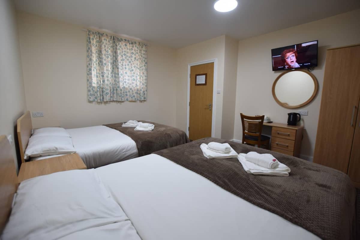 Quarto de hotel com duas camas, televisão, espelho, cadeira de madeira e escrivaninha.
