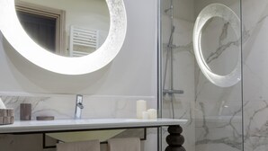 Uma casa de banho moderna com chuveiro em cabine de vidro, um espelho redondo e bancada de mármore.
