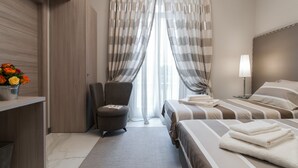 Quarto de hotel com cama, poltrona, escrivaninha e janela com cortinas.
