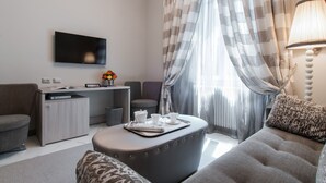 Quarto de hotel moderno com televisão de tela plana, escrivaninha com computador, sofá e janela com cortinas leves.