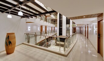 Interior de um hotel moderno com corrimão de vidro, uma escultura de madeira e uma escada que leva aos andares superiores.