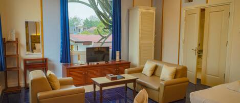 Quarto de hotel com sofá, cama, televisão, armário e janela com cortinas.