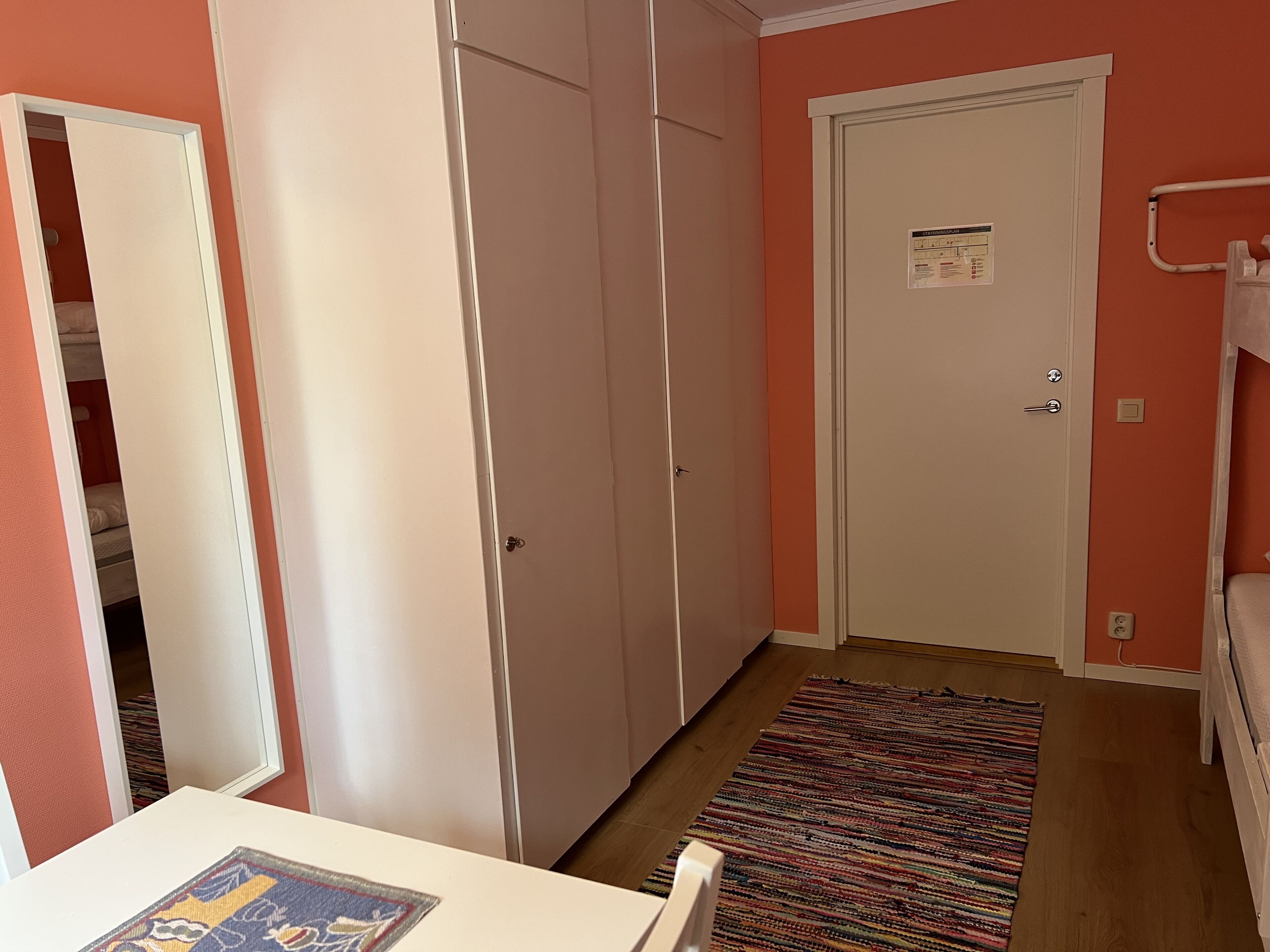 Quarto com cama, mesa de cabeceira, espelho e porta com um cartaz.