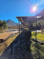 Uma estrutura movida a energia solar, com telhado de metal, cercada por um gramado com bancos e um rio.