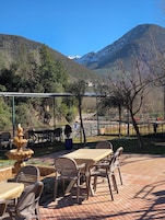 Uma área externa com mesas e cadeiras, uma fonte e vista para as montanhas.