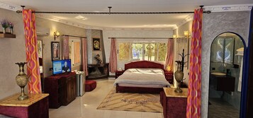 Um quarto espaçoso com uma cama grande, televisão, lareira e banheiro com espelho e pia.