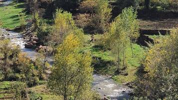 Paisagem montanhosa com rio, vegetação e edifícios tradicionais.