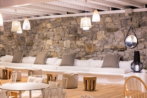 Uma área de estar moderna com parede de pedra, sofá branco, mesas de madeira e luminárias pendentes.
