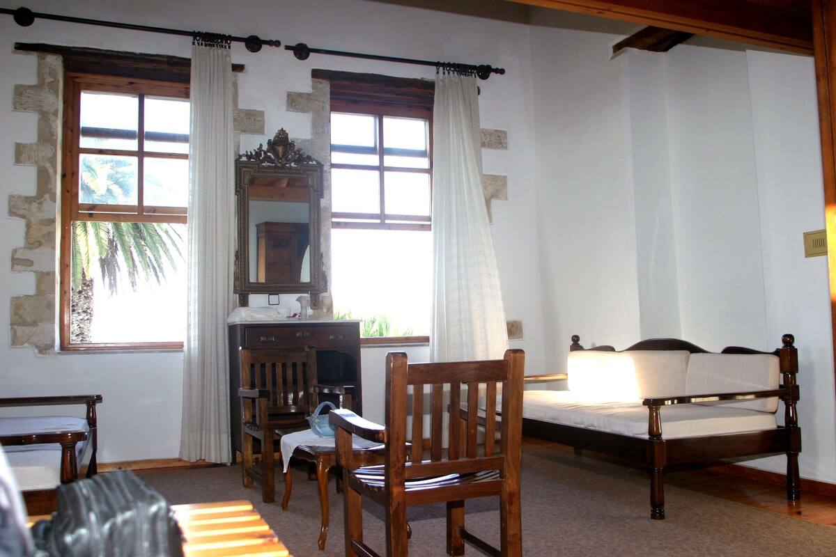 Um quarto com cama, uma cadeira de madeira, uma escrivaninha com cadeira e um espelho.