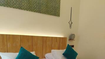 Cama bem arrumada com lençóis brancos, almofadas azul-esverdeadas e um arranjo floral sobre o cobreleito.