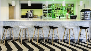 Uma área de bar moderna com balcão, banquetas e uma estante iluminada em verde exibindo garrafas.