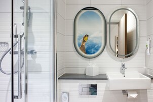 Casa de banho com chuveiro em cabine de vidro, lavatório e dois espelhos ovais com design de ganso.