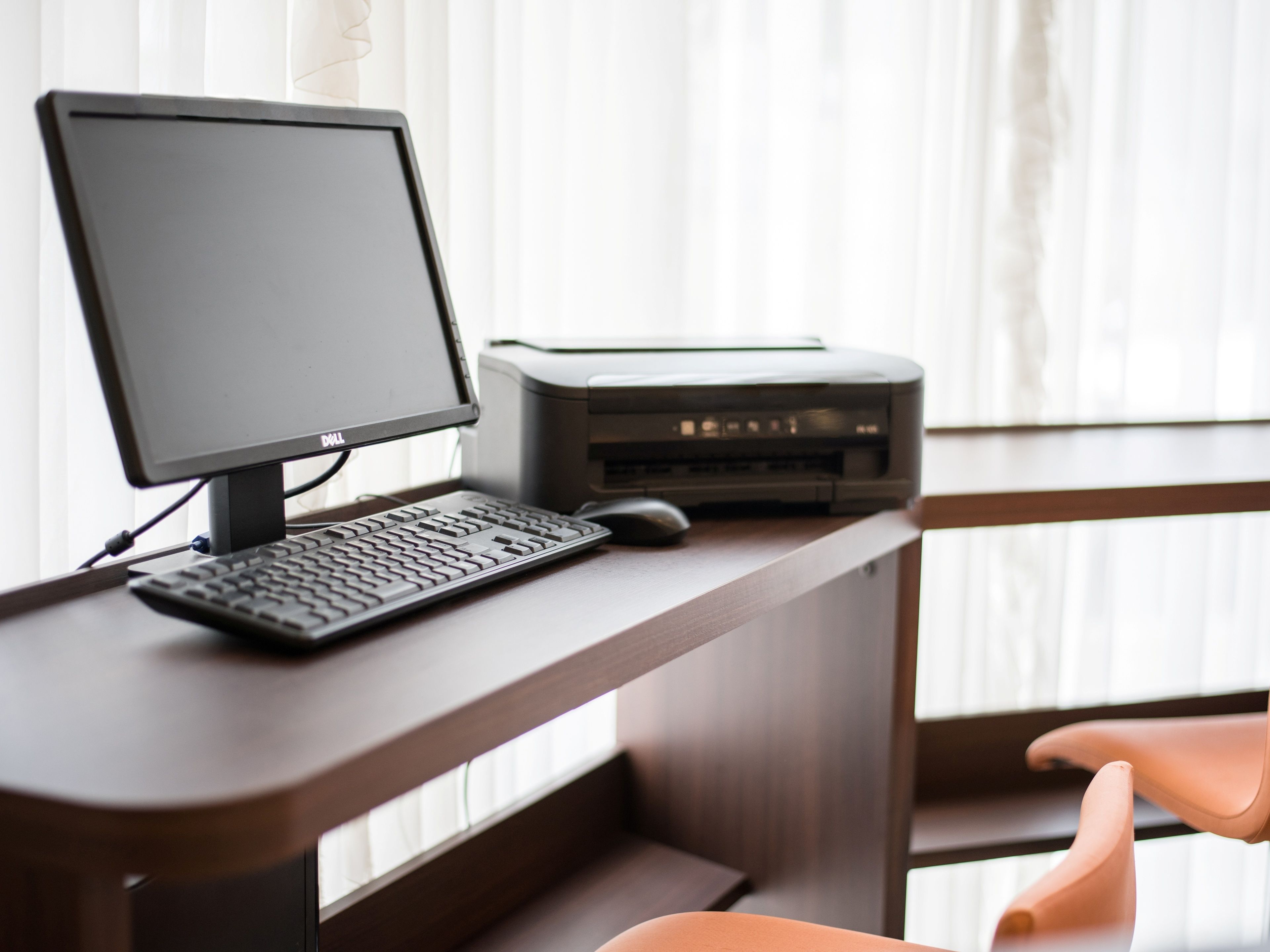 Uma mesa de escritório com monitor, teclado e impressora.