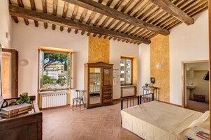 Quarto com cama, um armário de madeira, radiador, janela com vista e uma pequena mesa com cadeira.
