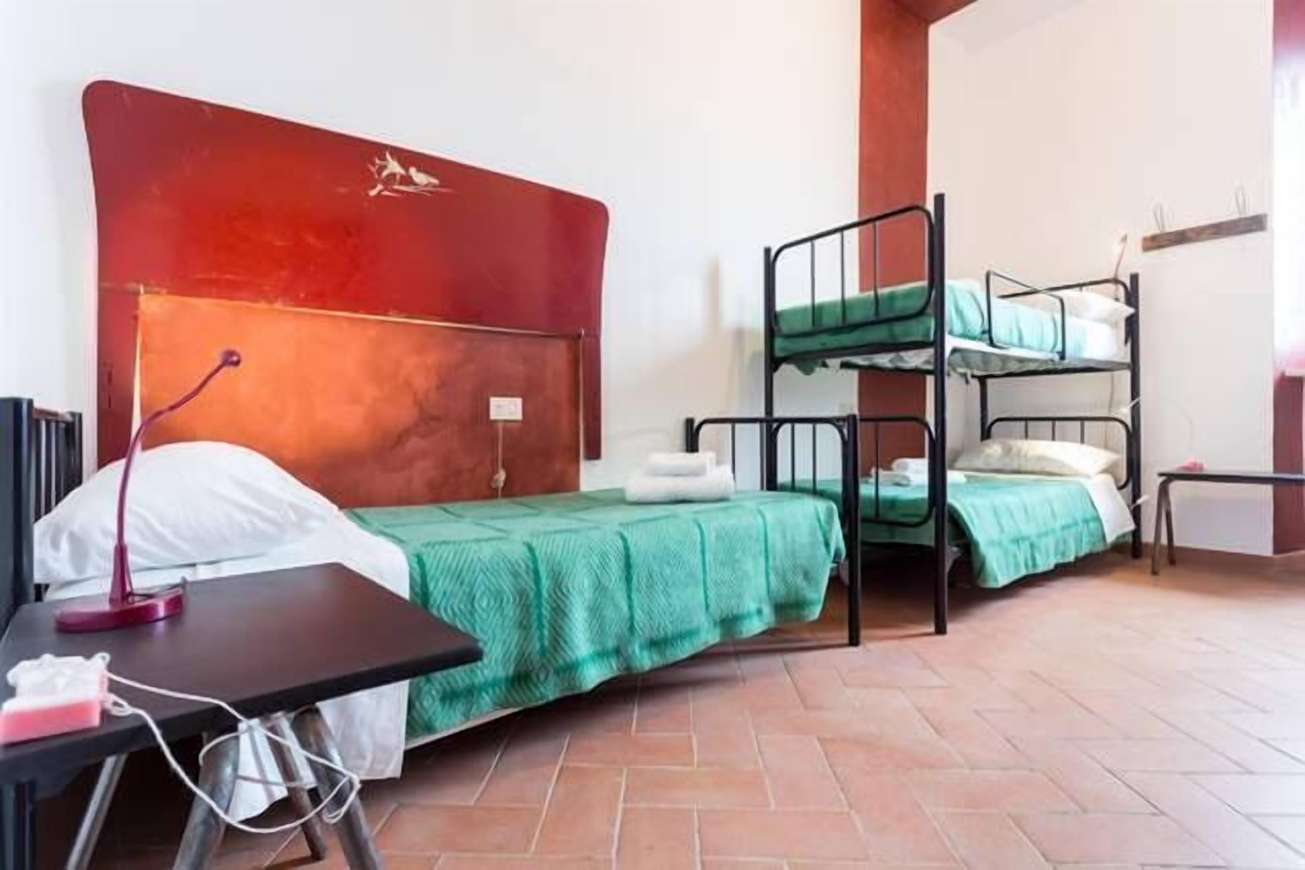 Quarto tipo dormitório com beliches, uma escrivaninha com luminária e piso ladrilhado.