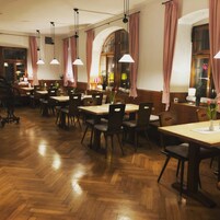 Um restaurante com piso de madeira, várias mesas e cadeiras, e luminárias pendentes.