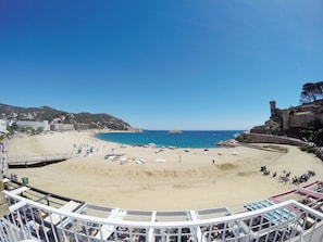 Uma praia com vista clara para o mar, areal arenoso e uma estrutura de pedra histórica.