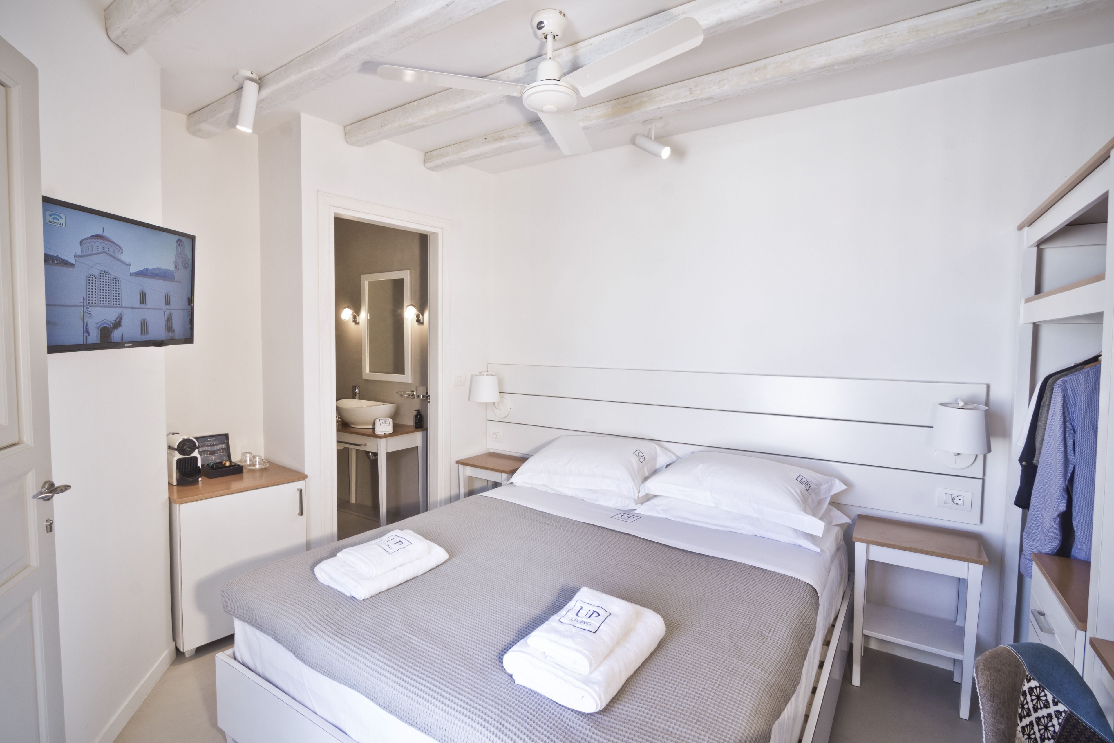 Quarto de hotel com cama, mesas de cabeceira, televisão, banheiro e guarda-roupa.