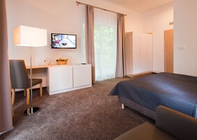 Quarto de hotel com cama, escrivaninha com cadeira, televisão e armário.
