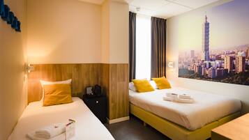 Quarto de hotel com duas camas, cabeceira de madeira, painel com um mural da paisagem urbana e uma janela com cortinas.