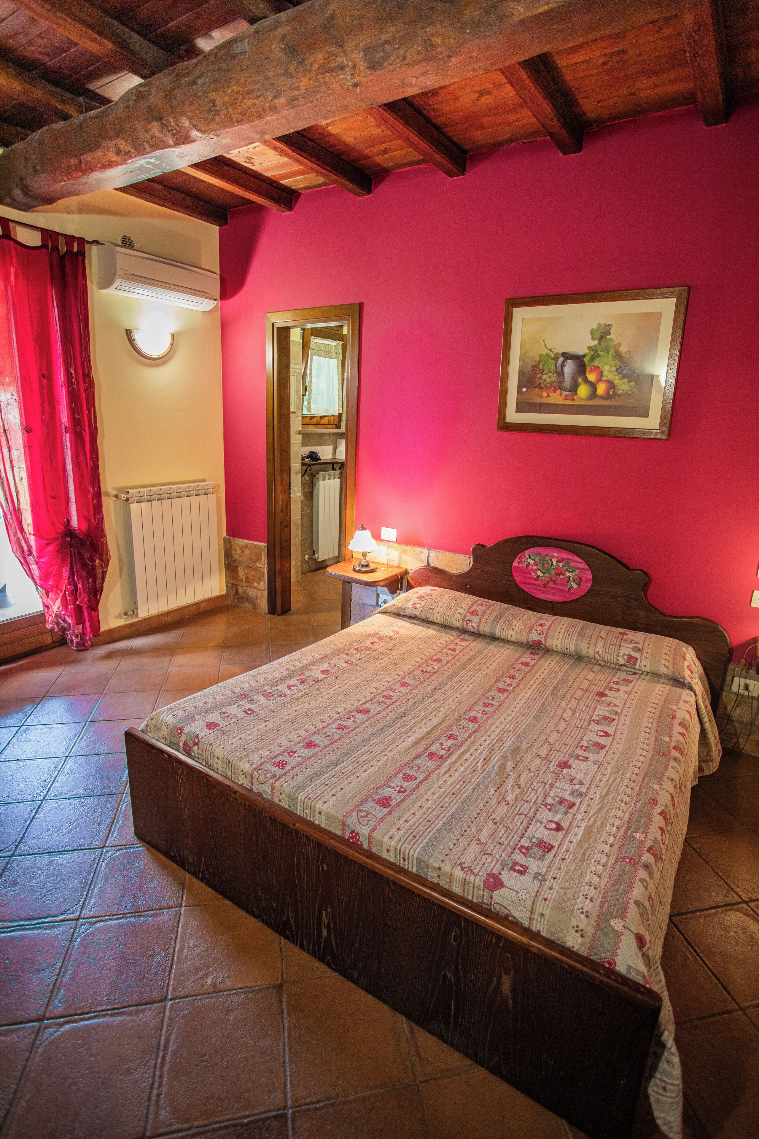 Quarto com cama, mesa de cabeceira, espelho e janela com cortinas.