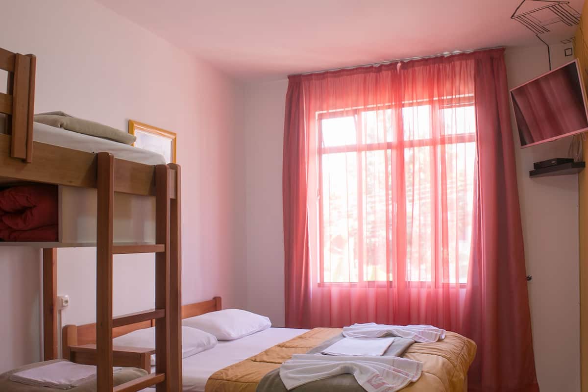Um dormitório com beliches, uma cama de solteiro, uma janela com cortinas cor-de-rosa e uma luminária no teto.