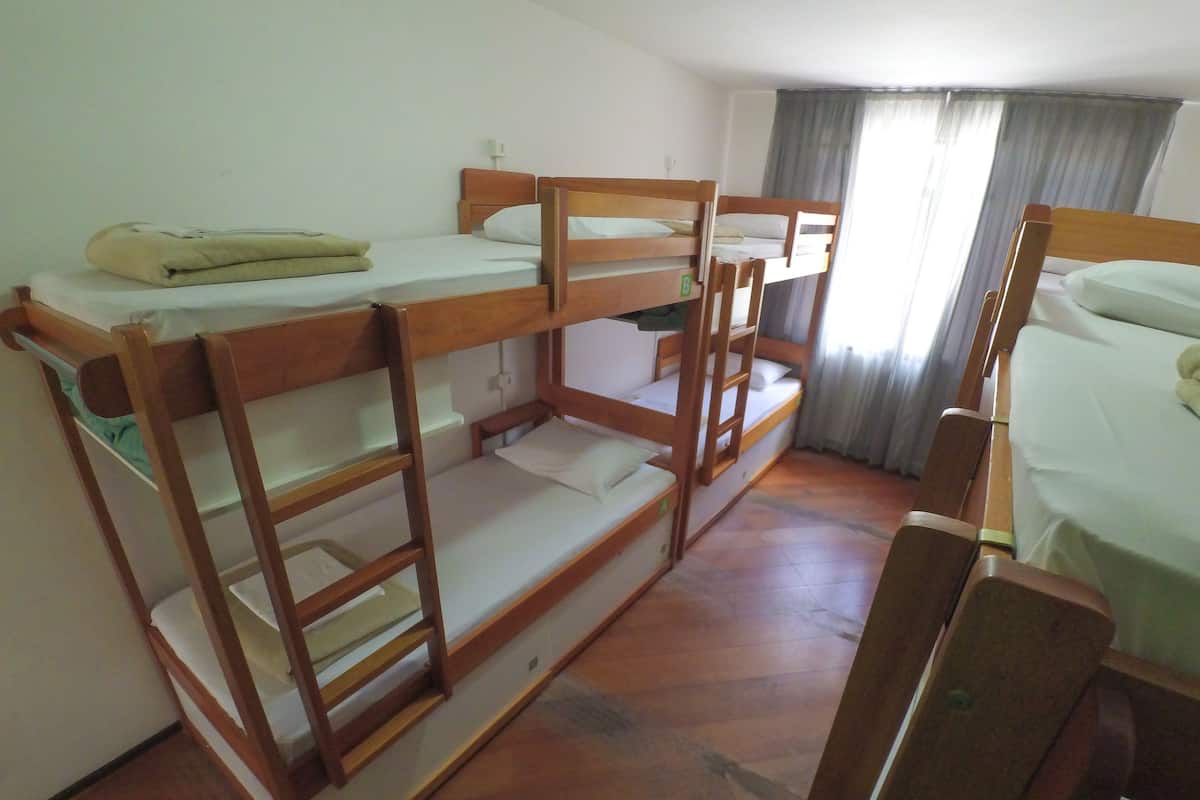 Quarto com beliches, mobiliário de madeira e janela com cortinas.