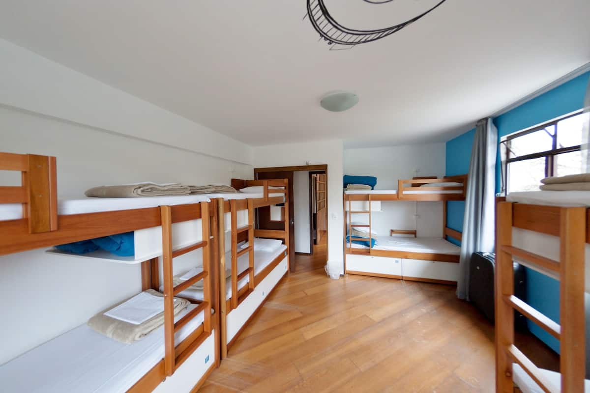 Um dormitório com beliches, piso de madeira e janela com cortinas.