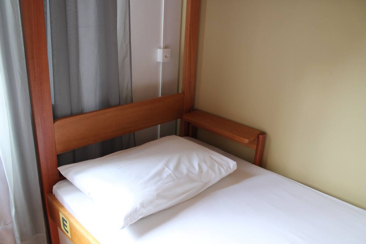 Uma cama de solteiro com cabeceira de madeira e colchão branco.